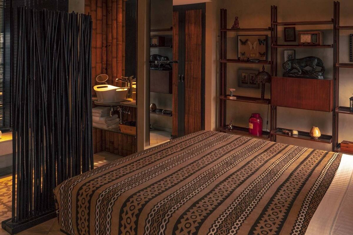 Quarto com colcha estampada, guarda-roupa de madeira e uma prateleira com objetos decorativos.