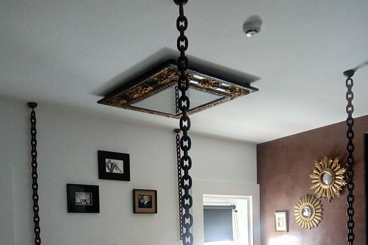 Uma cama com dossel e cortinas em trama de corrente, roupa de cama branca e chão com padrão geométrico.