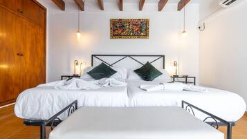 Uma cama de casal com roupa de cama branca, duas mesas de cabeceira com luminárias, teto de madeira e um adorno colorido na parede.