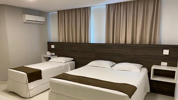 Quarto de hotel com duas camas, uma mesa de cabeceira e um aparelho de ar condicionado.