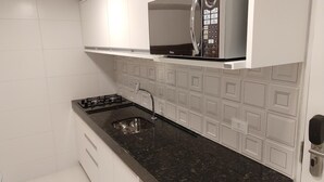 Uma cozinha moderna com armários brancos, bancada de granito preto, fogão a gás e micro-ondas sobre a pia.