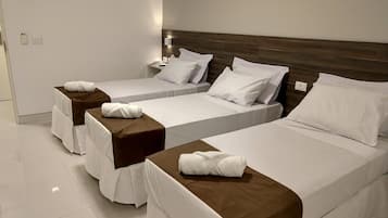 Quarto de hotel com três camas de solteiro, cada uma com cabeceira marrom e roupa de cama branca.
