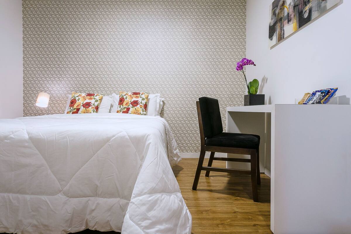 Quarto bem arrumado com uma cama, uma escrivaninha e uma cadeira.