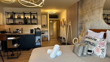 Quarto de hotel moderno com uma cama grande, uma kitchenette e um espaço de refeições.