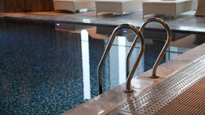 Uma área de piscina com guarda-corpos de metal e espreguiçadeiras com almofadas.