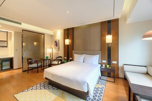 Quarto de hotel com cama, mesas de cabeceira, escrivaninha, cadeira e um pequeno frigorífico.