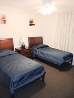 Quarto de hotel com duas camas de solteiro, mesa de cabeceira com abajur e ventilador de teto.