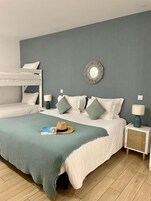 Quarto com uma cama de solteiro, uma cama grande com várias almofadas, um espelho, abajures e um chapéu na cama.