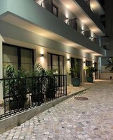 Exterior de hotel com pátio pavimentado, vasos de plantas e design moderno.