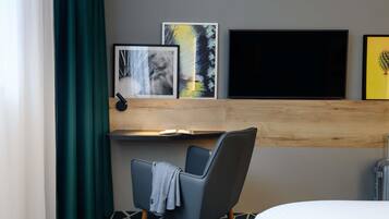 Quarto de hotel com cama, escrivaninha com cadeira, televisão e obras de arte na parede.