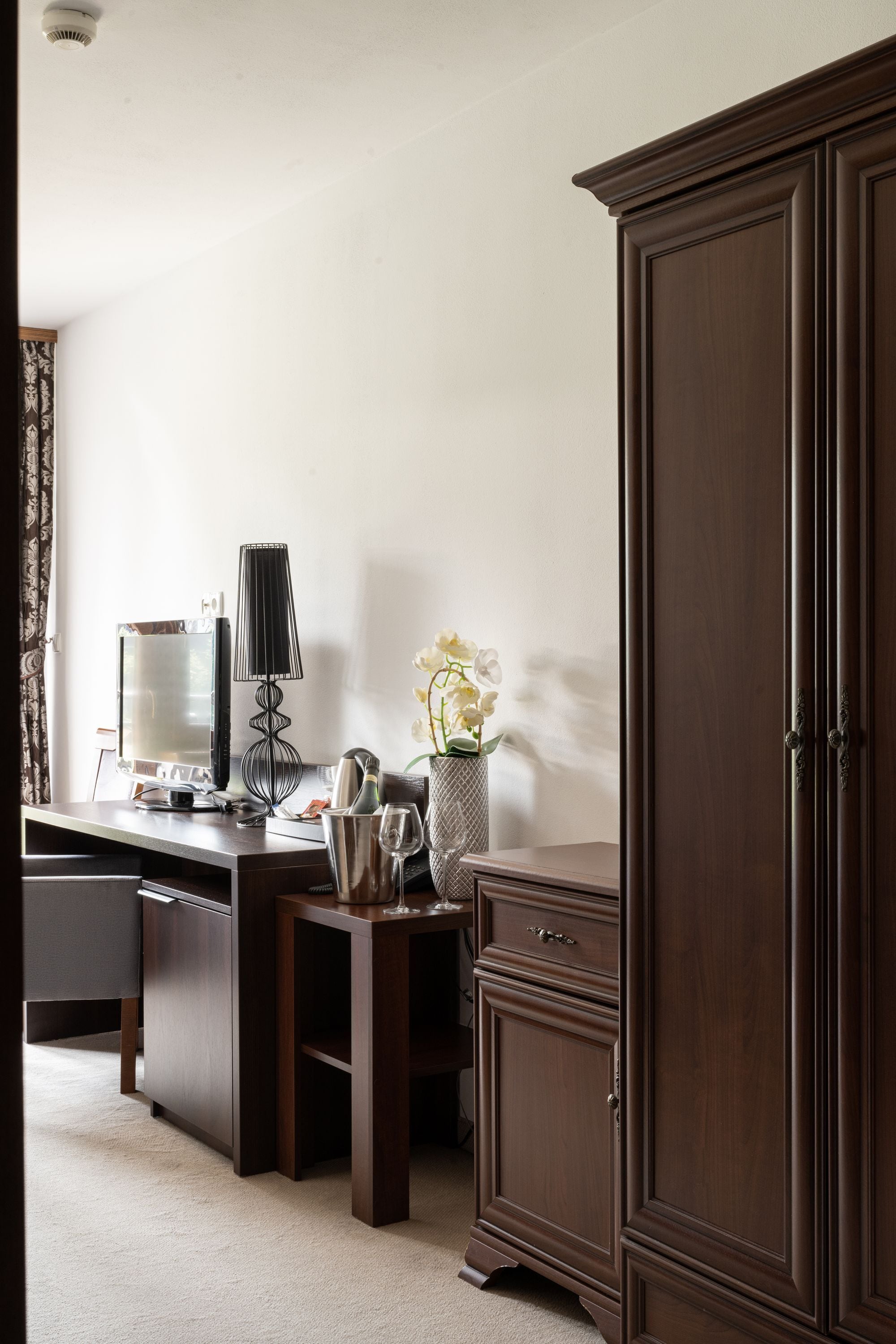 Um quarto com escrivaninha, luminária, um vaso com flores e um armário.