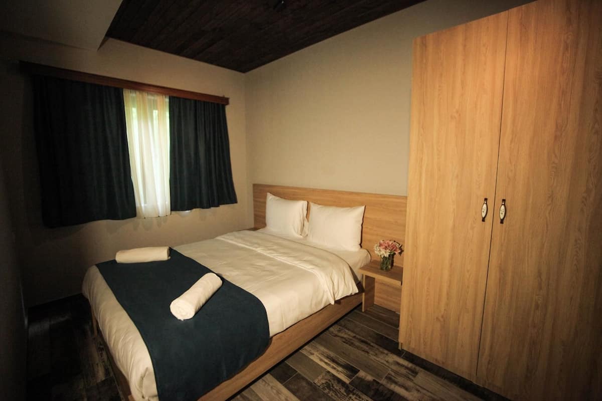 Quarto de hotel com cama de madeira, mesa de cabeceira com um vaso de flores e um guarda-roupa.