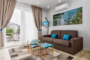 Uma sala de estar moderna com um sofá marrom, almofadas azuis, um abajur azul e uma grande pintura de paisagem na parede.