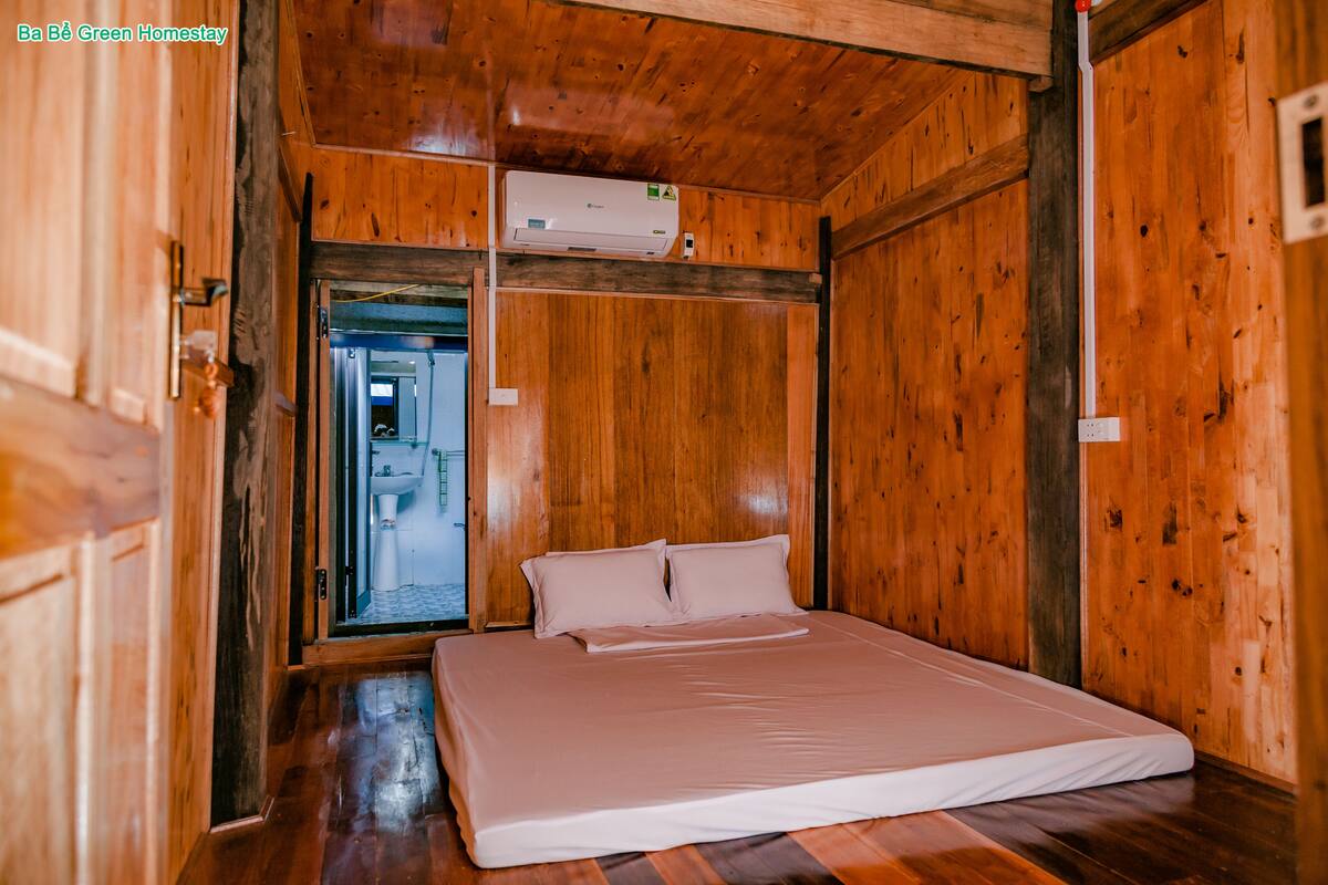 Quarto de madeira com cama, ar condicionado e banheiro à vista.