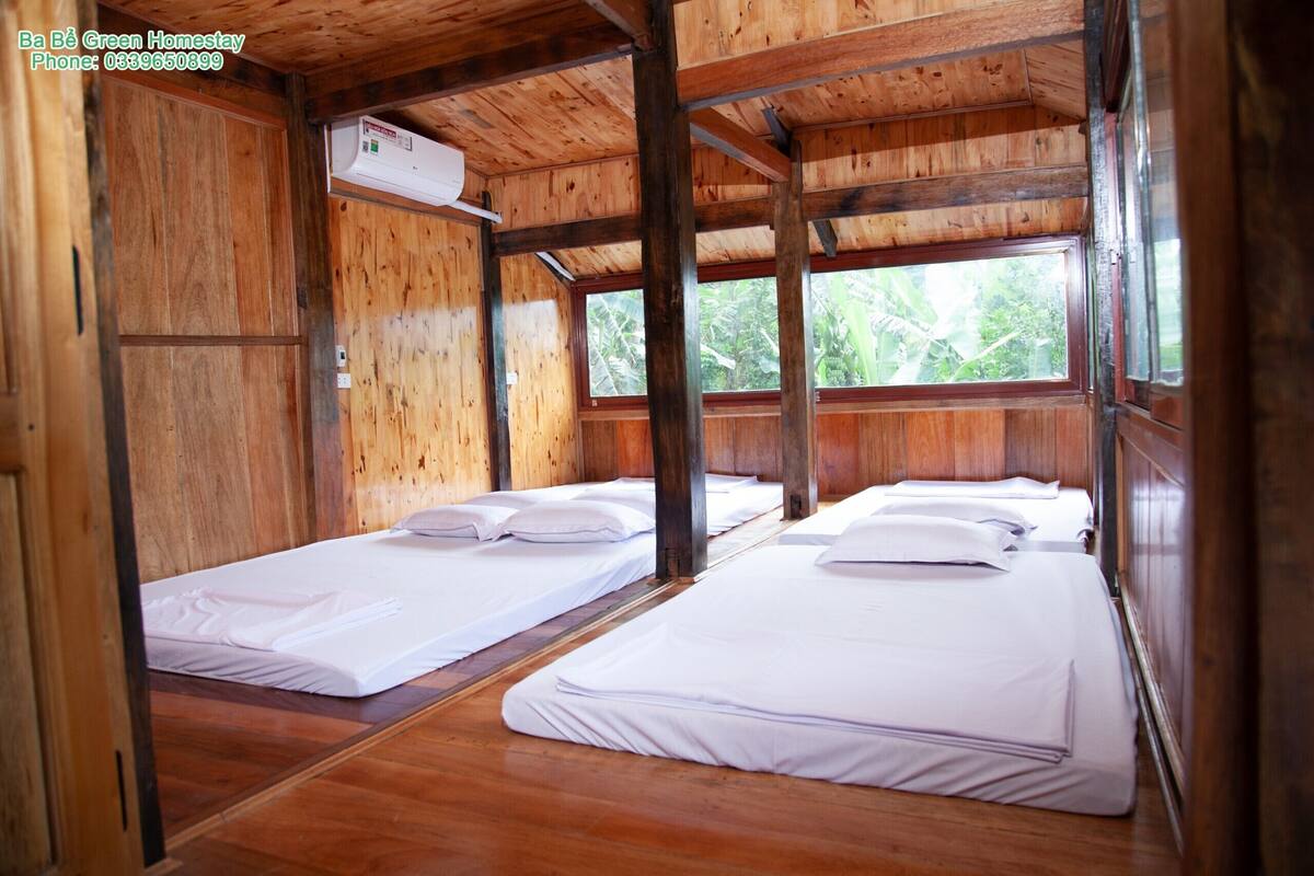 Uma cabana de madeira com duas camas de solteiro, cada uma com lençóis e almofadas brancas, e uma janela com vista para o verde lá fora.