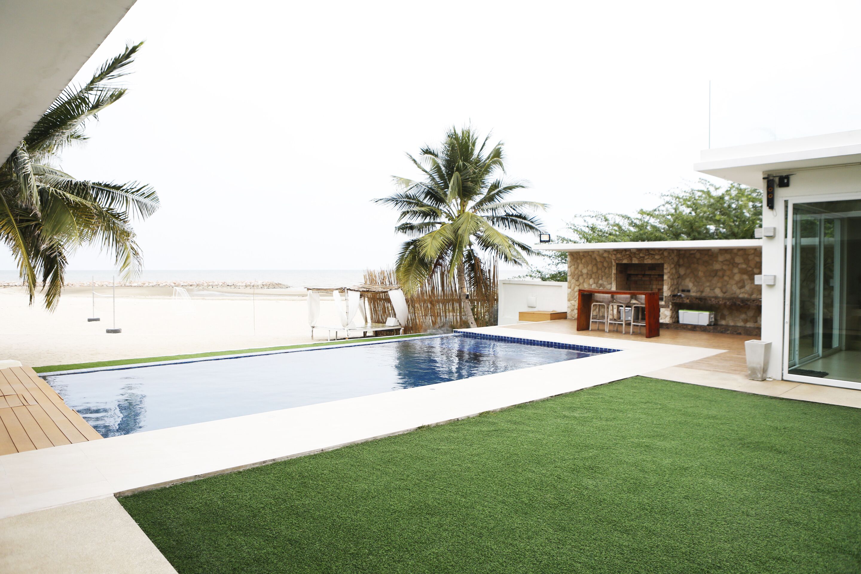 Uma área moderna de piscina ao ar livre com grama sintética, uma parede de pedra e um espaço de estar com mesa e cadeiras.