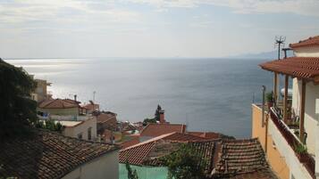 Uma vila costeira com edifícios de telhados em tons de terracota, vista para o mar e céu claro.