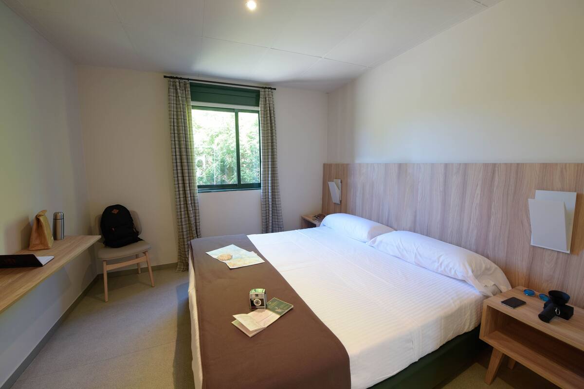Quarto de hotel com uma cama grande, uma escrivaninha, uma cadeira e uma janela com cortinas.