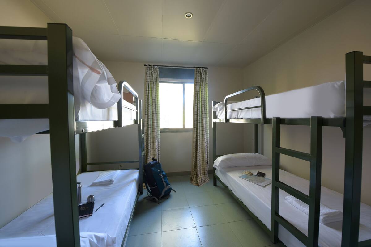 Um quarto de dormitório com beliches, uma janela com cortinas e uma mochila no chão.