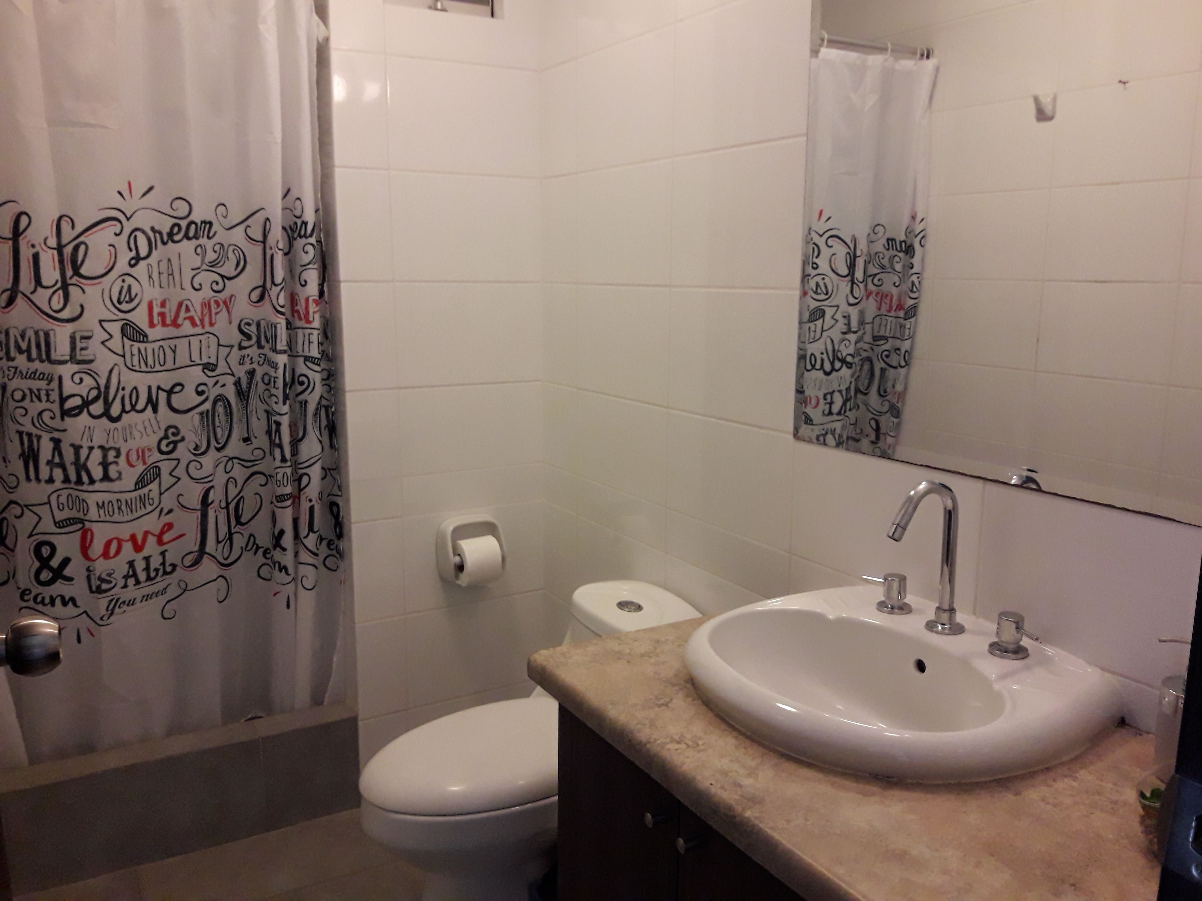 Uma casa de banho com sanita branca, lavatório e cortina de chuveiro com frases motivacionais.