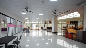 Amplo espaço interno, bem iluminado, com ventiladores de teto, mesas, cadeiras e uma escada.