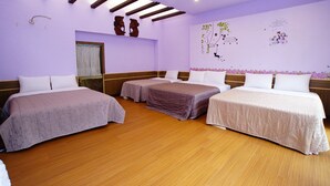 Quarto de hotel com três camas, piso de madeira e ventilador de teto.