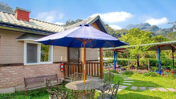 Uma casa com varanda coberta, mesa de pátio e um guarda-sol azul.