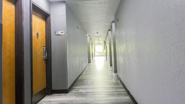 Um corredor comprido e estreito com portas de madeira à esquerda e uma placa indicando o quarto 222.