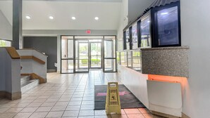 Um hall de hotel com escadas, balcão de recepção e entrada por porta de vidro.