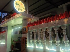 Um edifício com uma placa indicando um estabelecimento comercial no andar térreo. Há vários contêineres vermelhos no nível superior e uma fileira de vasos brancos no nível inferior.