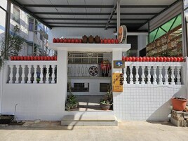 Entrada de um edifício com fachada em azulejos, varanda com vasos decorativos e uma placa.