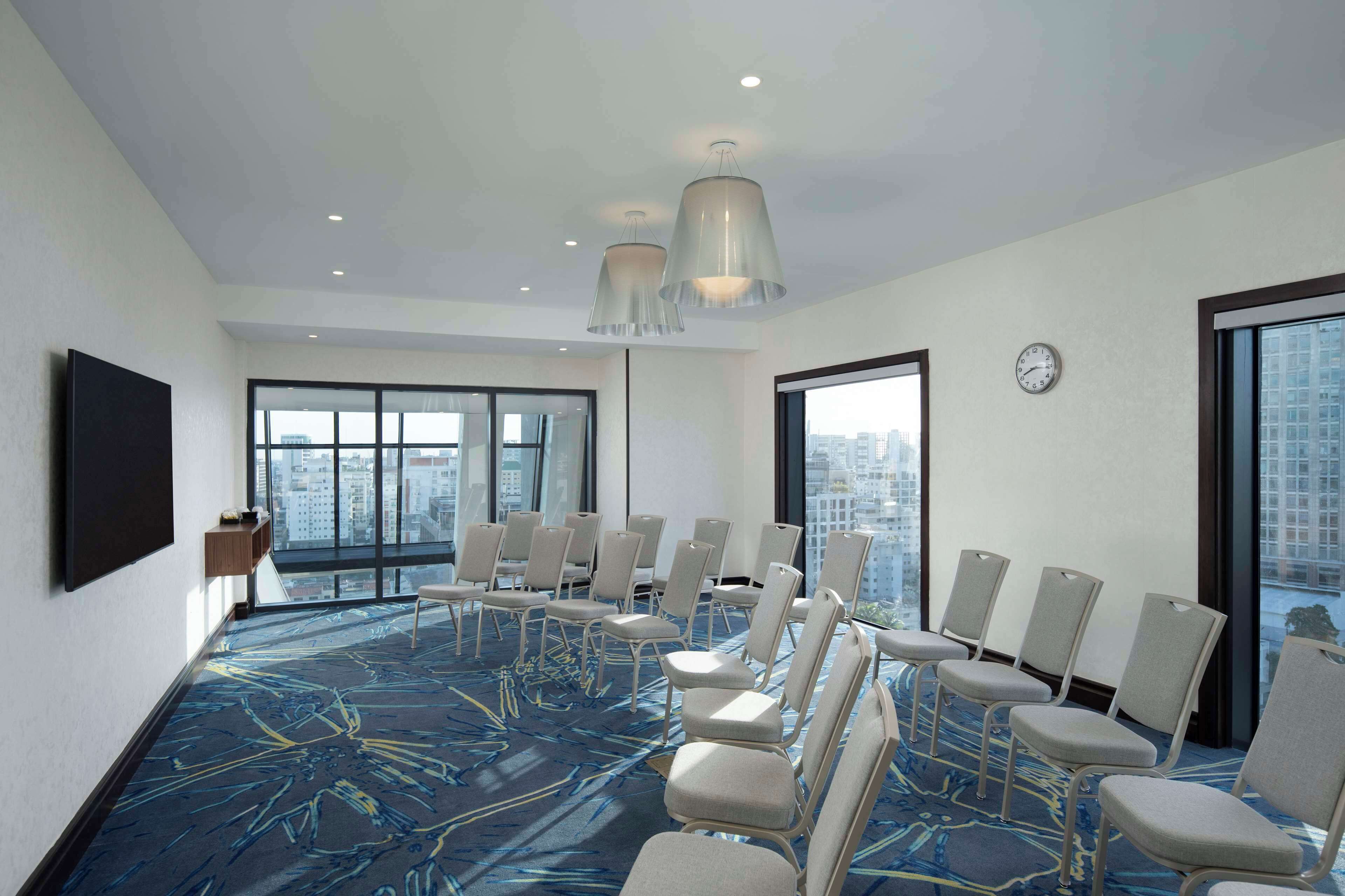 Uma sala de conferências com uma mesa grande, várias cadeiras e amplas janelas com vista para a cidade.