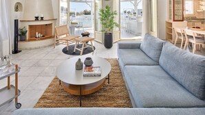 Uma sala de estar moderna com um sofá cinzento, uma mesa de centro redonda com livros e vasos, uma lareira e vista para o exterior.