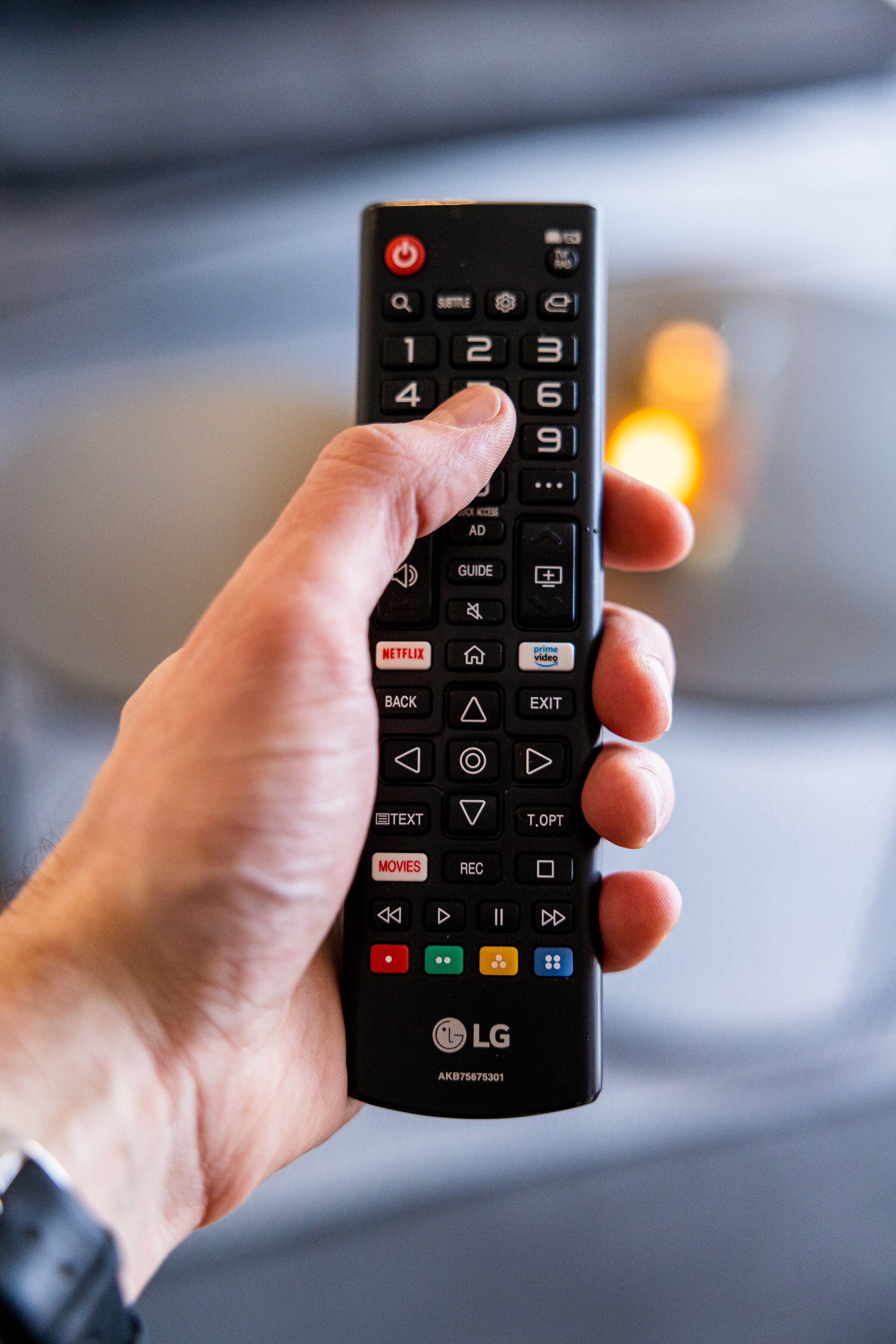 Uma mão segurando um controle remoto com diversos botões e ícones, incluindo Netflix e Prime Video.