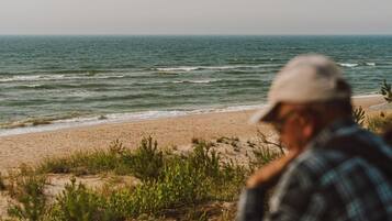 Uma praia com uma pessoa sentada num corrimão, apreciando a vista do oceano.