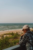 Uma praia com uma pessoa sentada num corrimão, apreciando a vista do oceano.
