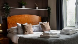 Uma cama bem arrumada com almofadas, uma mesa de cabeceira com abajur e uma janela com cortinas.