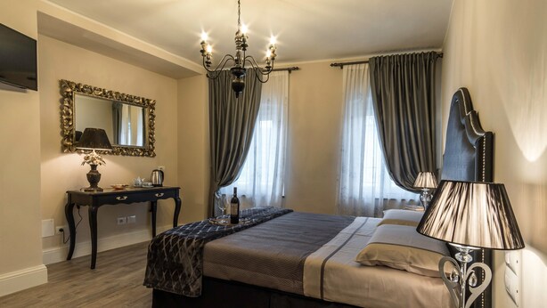 Quarto de hotel com uma cama grande, uma mesa de cabeceira com abajur, cômoda, espelho e um candelabro.