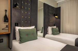 Quarto de hotel com duas camas, um espelho, uma bolsa pendurada e uma luminária na parede.