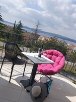 Uma varanda com mesa e cadeiras, uma garrafa de vinho e vista para um lago e montanhas.