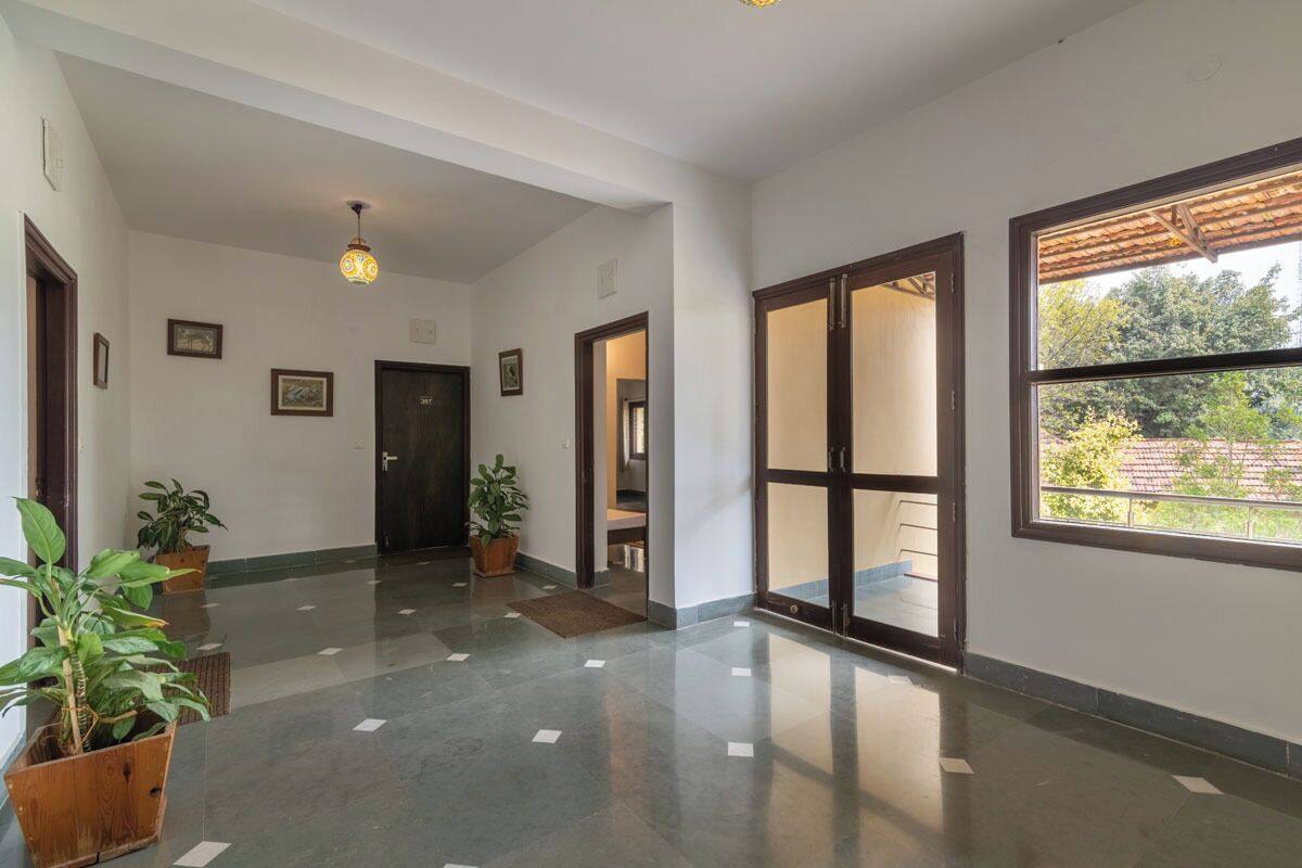 Corredor com piso lustroso, plantas em vasos, uma porta e uma janela com vista para o verde.