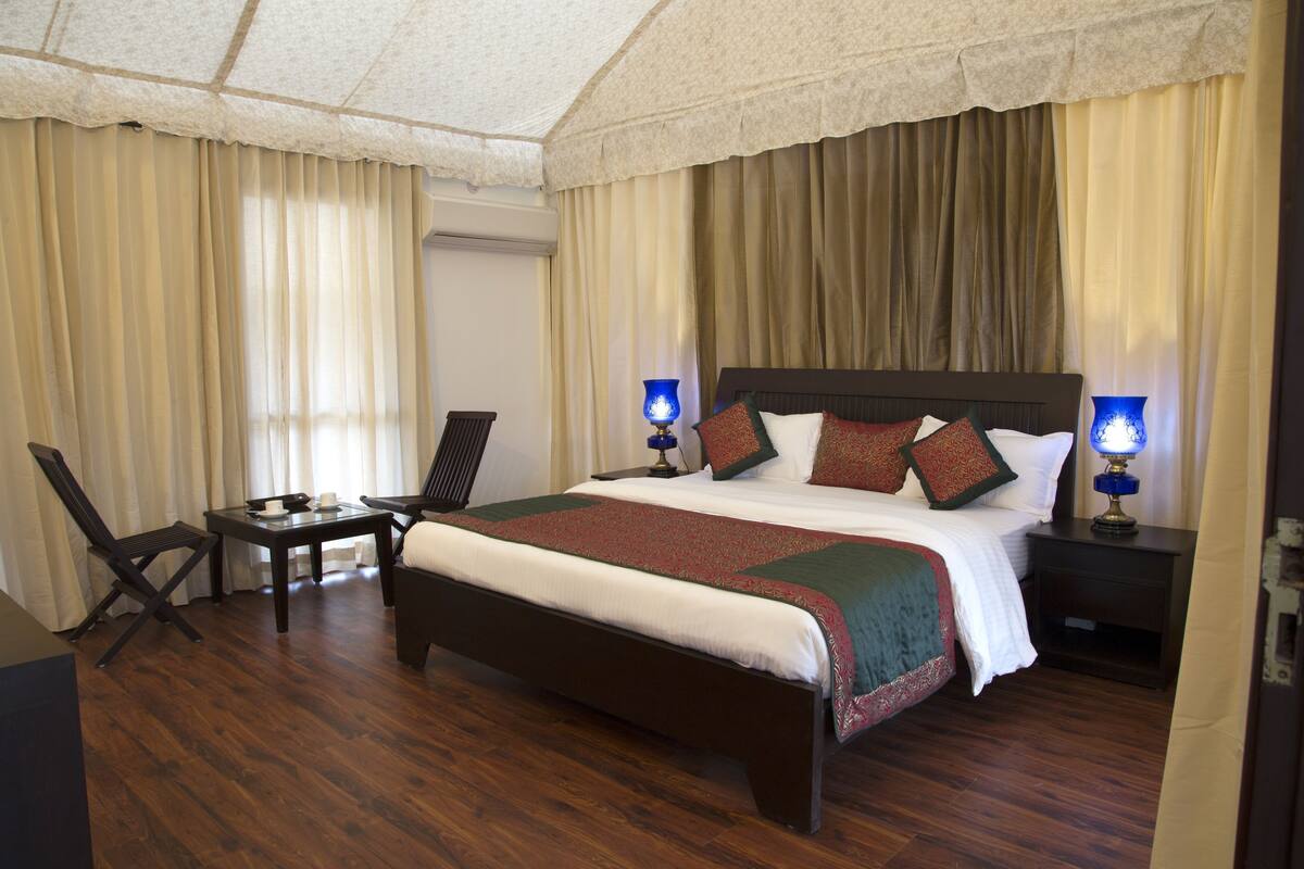 Quarto de hotel com uma cama grande, duas mesas de cabeceira com abajures, uma cadeira e uma pequena mesa.