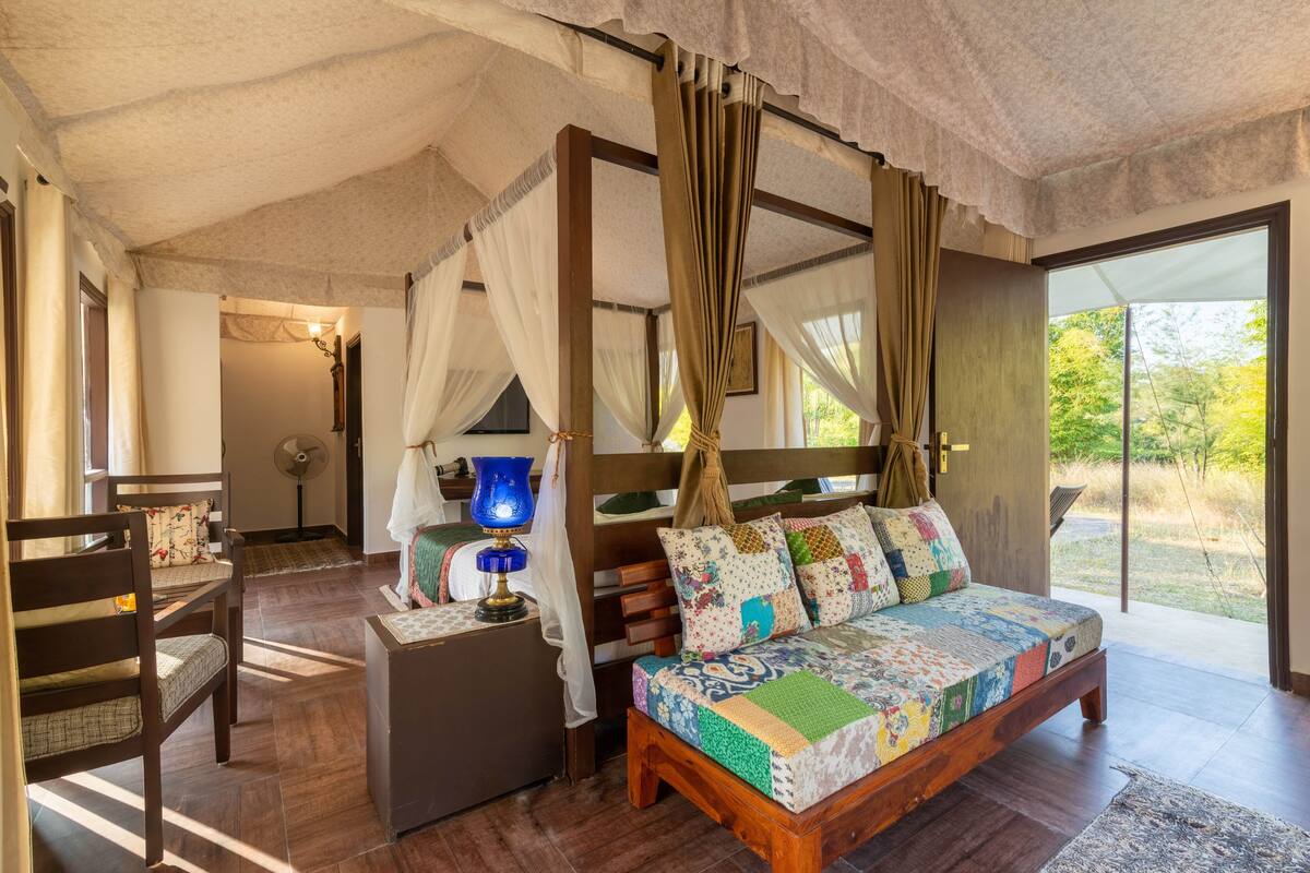 Um quarto espaçoso com uma cama grande, uma cadeira de madeira, uma mesinha de cabeceira com abajur e vista para o exterior.