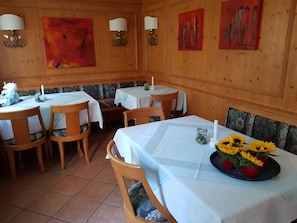 Uma sala de jantar com painéis de madeira, toalhas de mesa brancas e almofadas florais.