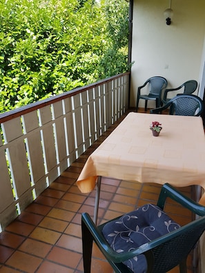 Um pátio com mesa e cadeiras, cerca branca e folhagem verde ao fundo.