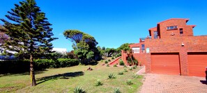 Um edifício com fachada de tijolos vermelhos, uma garagem e um gramado bem cuidado com diversas plantas.