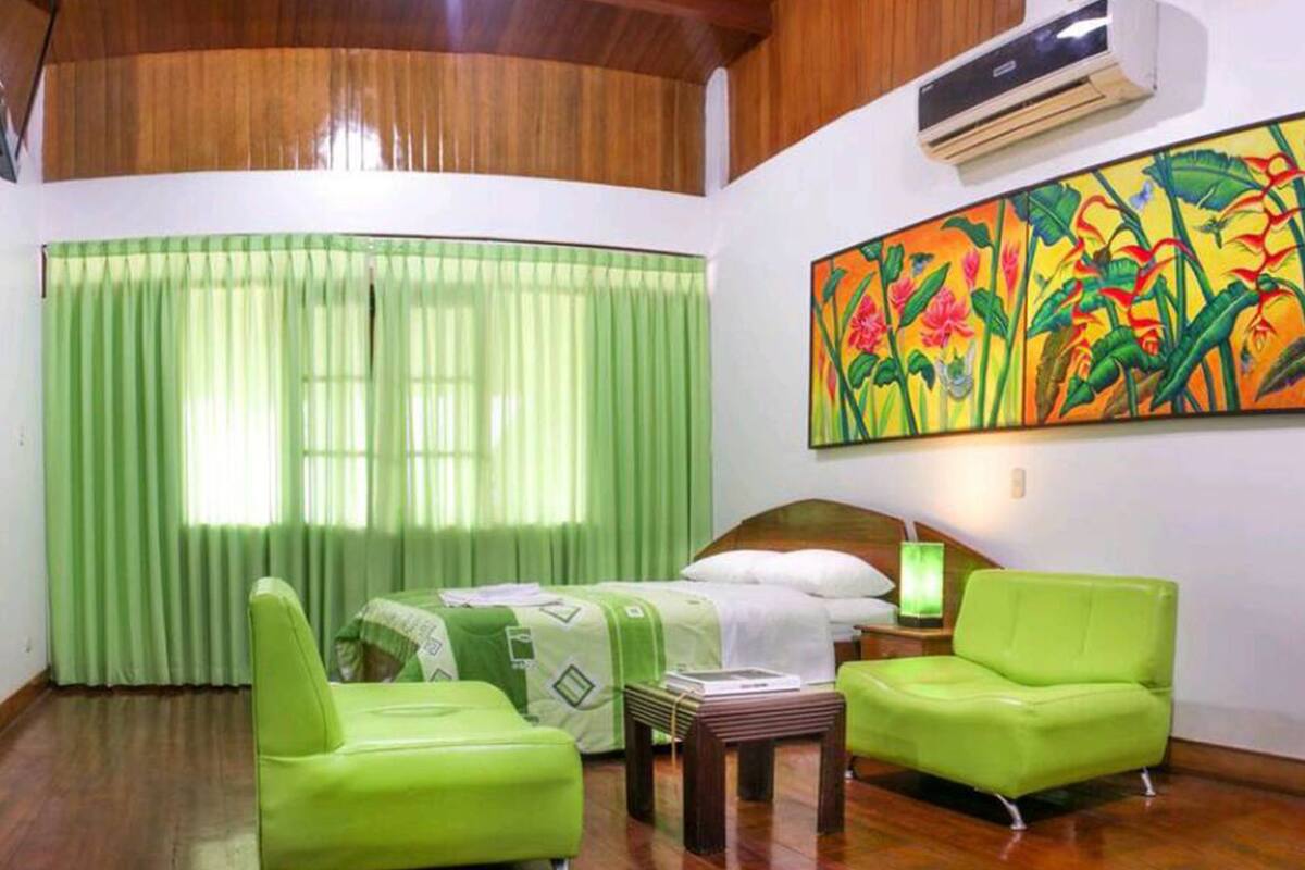 Quarto com uma cama, duas cadeiras verdes, um quadro e teto de madeira.