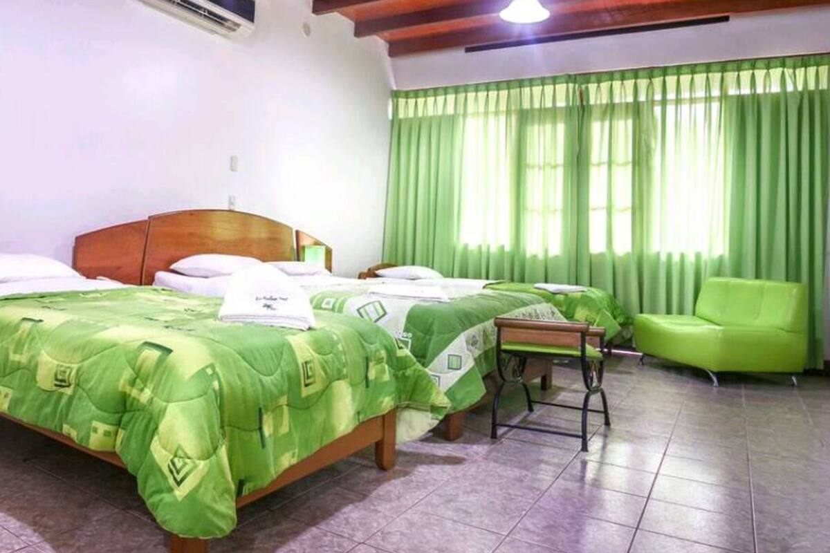 Quarto de hotel com duas camas, uma cadeira verde e uma pequena mesa.
