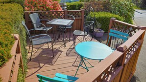 Um deck de madeira com móveis de exterior, incluindo uma mesa e cadeiras, rodeado por vegetação e uma cerca de madeira.