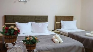 Quarto de hotel com duas camas, uma mesa de cabeceira de madeira, um relógio branco e cestos de flores.